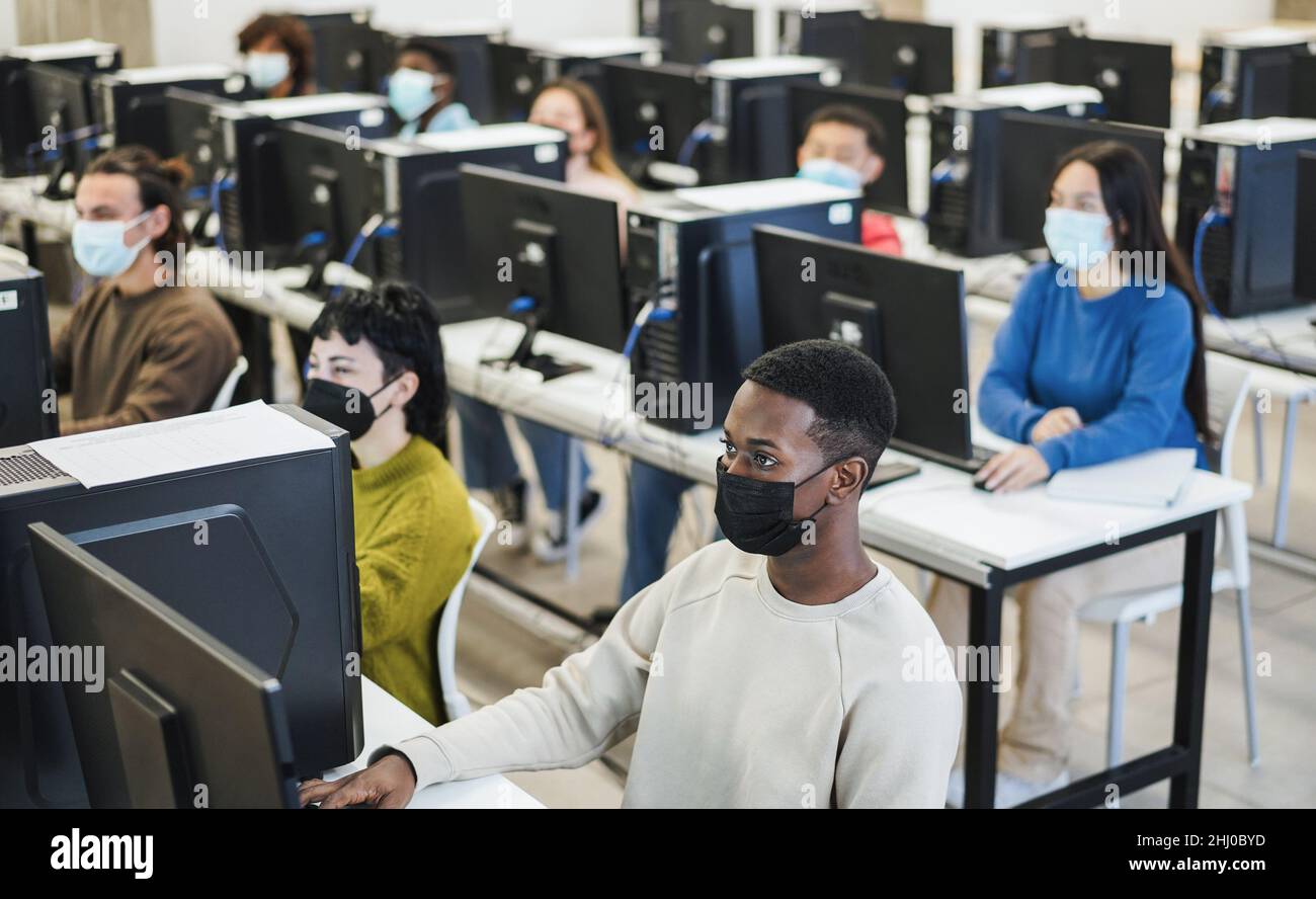 Young multiracial students using computers wearing protective mask ...