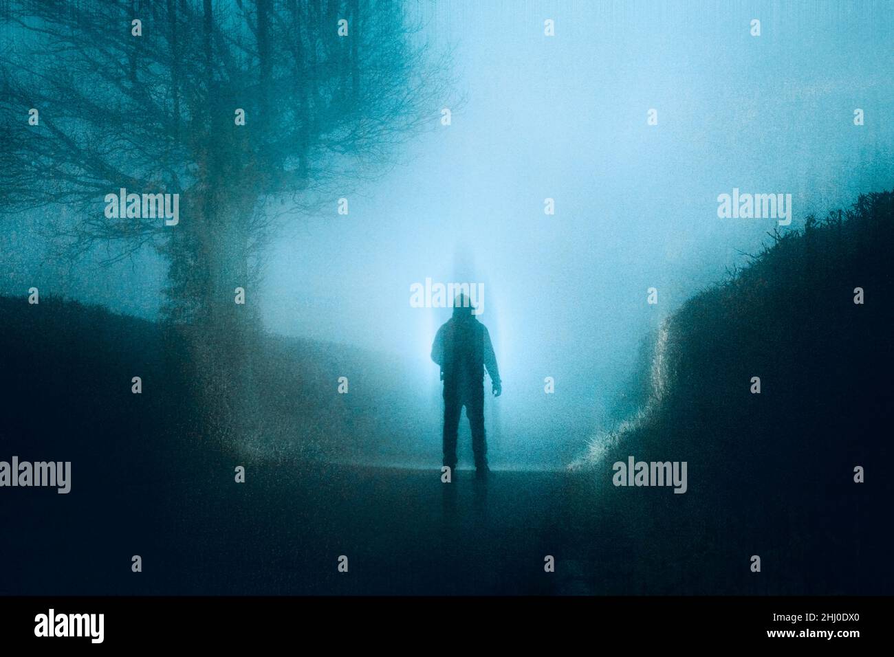 A spooky concept of a figure shining a torch on a country road. On a ...