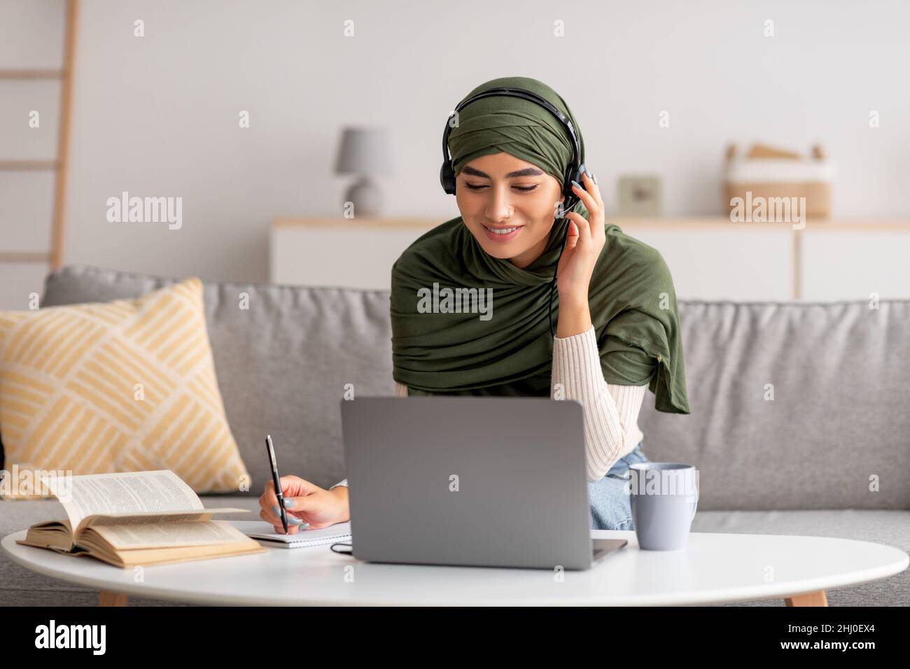 Millennial Arab woman in hijab using laptop, wearing headphones, taking ...