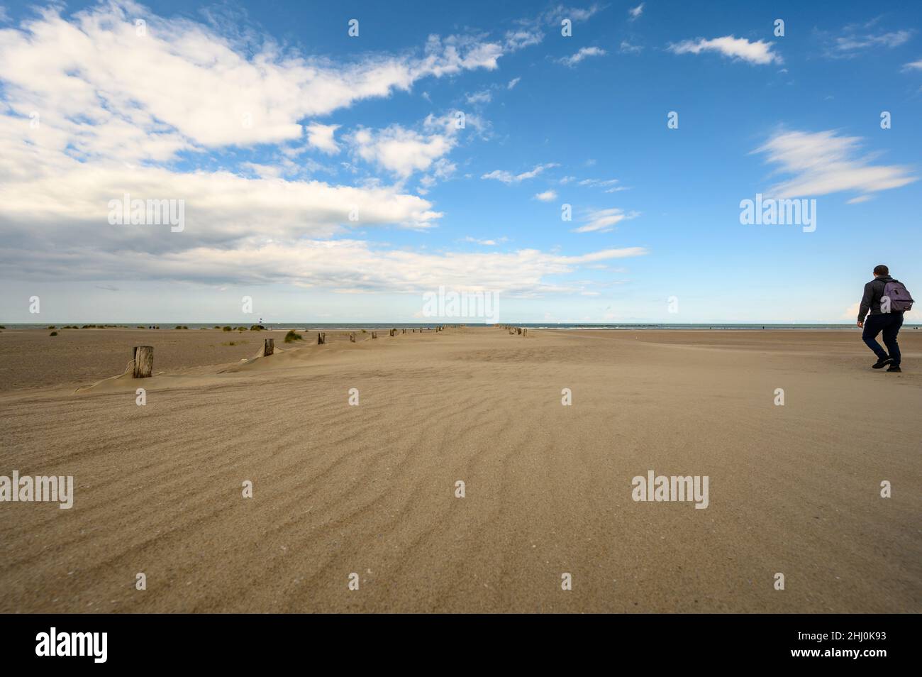 Backpacker walks along beach at Dunkirk with wooden poles of the sea ...