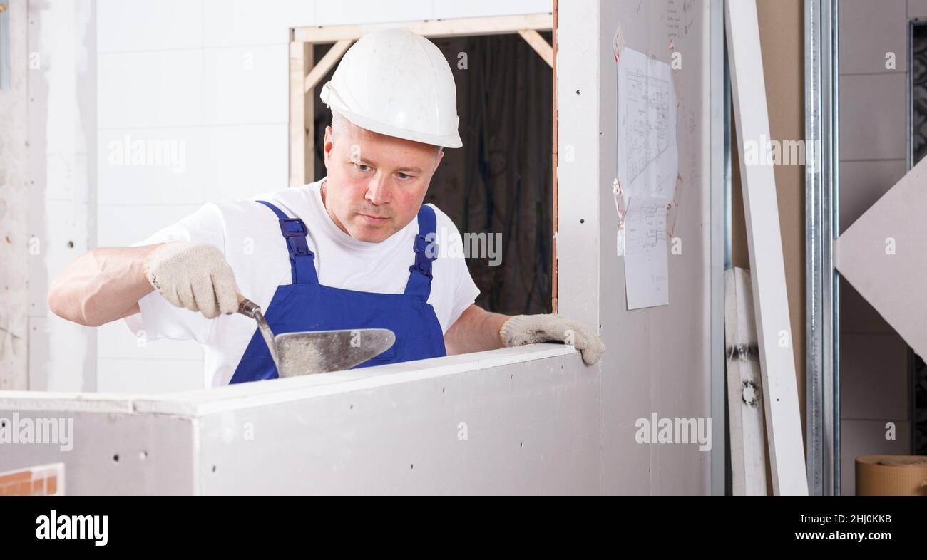 Builder filling gaps on drywall element Stock Photo - Alamy