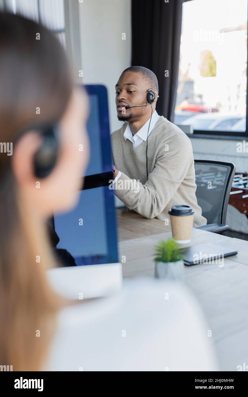 african american operator in headset talking near blurred colleague in ...