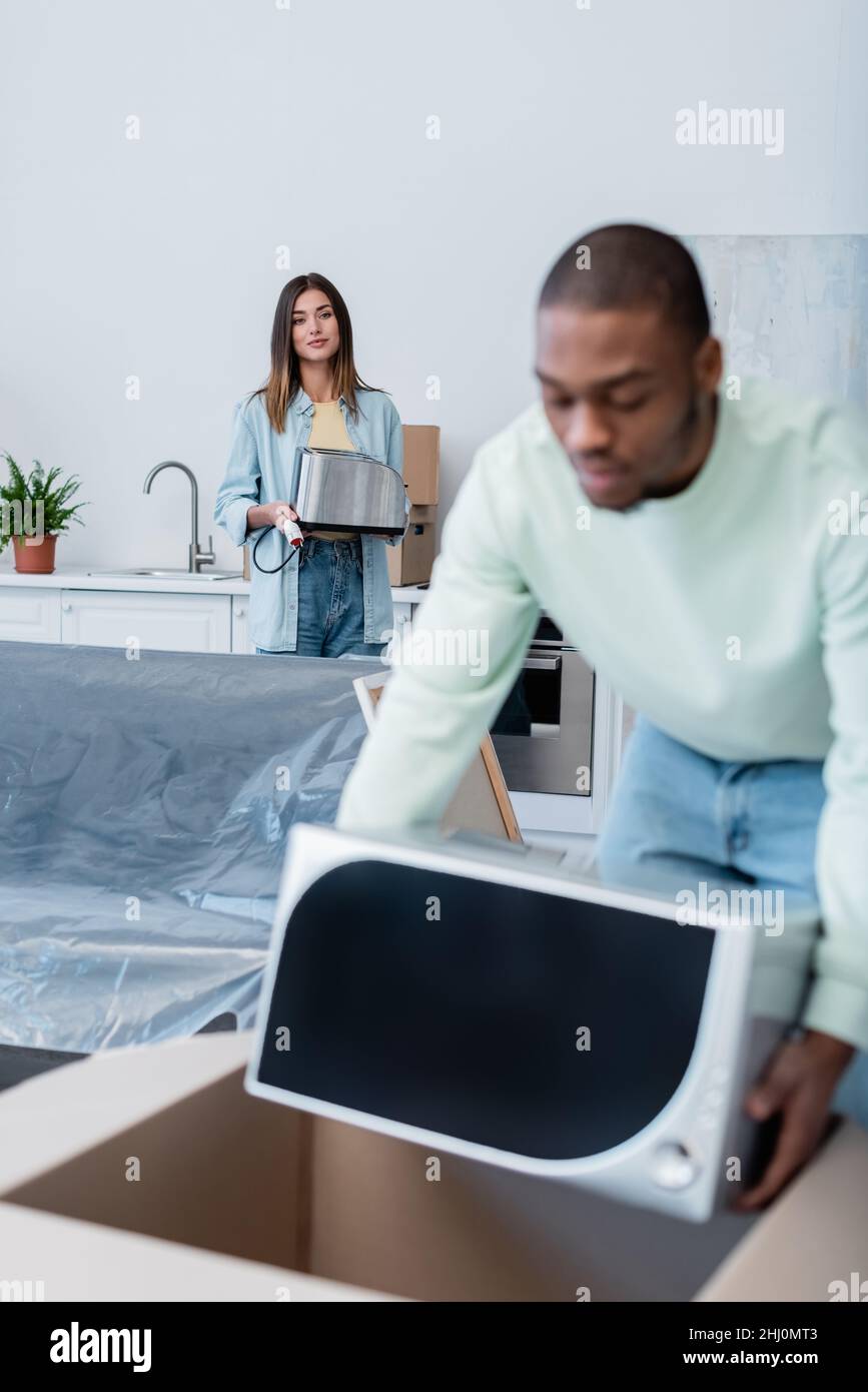 happy woman holding toaster and looking at blurred african american man ...
