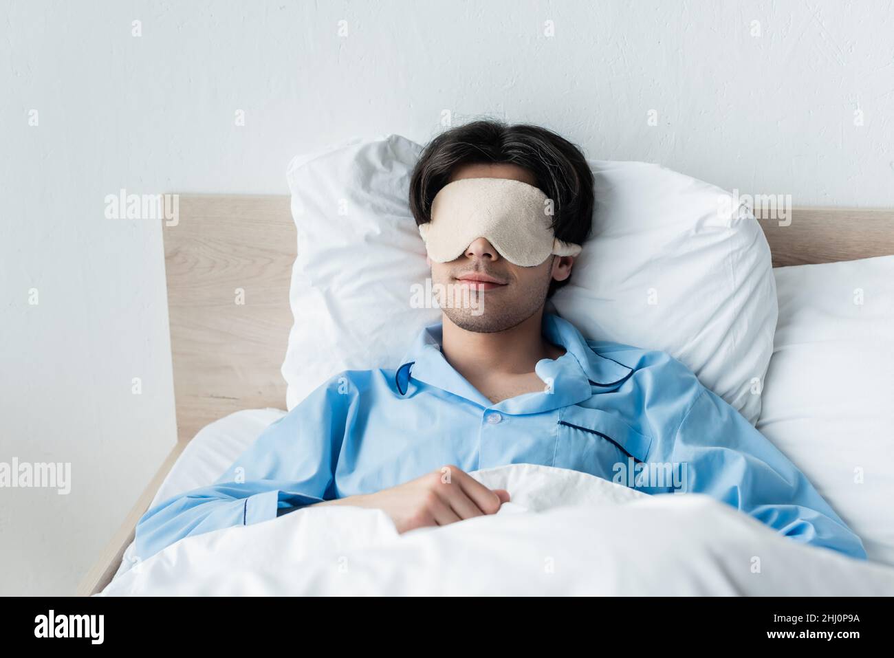 brunette man in blue pajamas and sleep mask lying on white bedding Stock Photo - Alamy