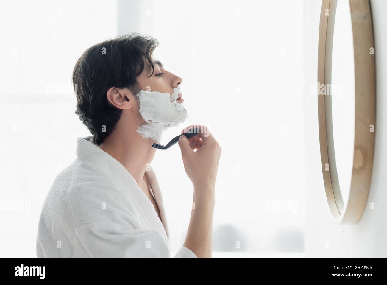 side view of brunette man shaving near mirror in bathroom Stock Photo ...