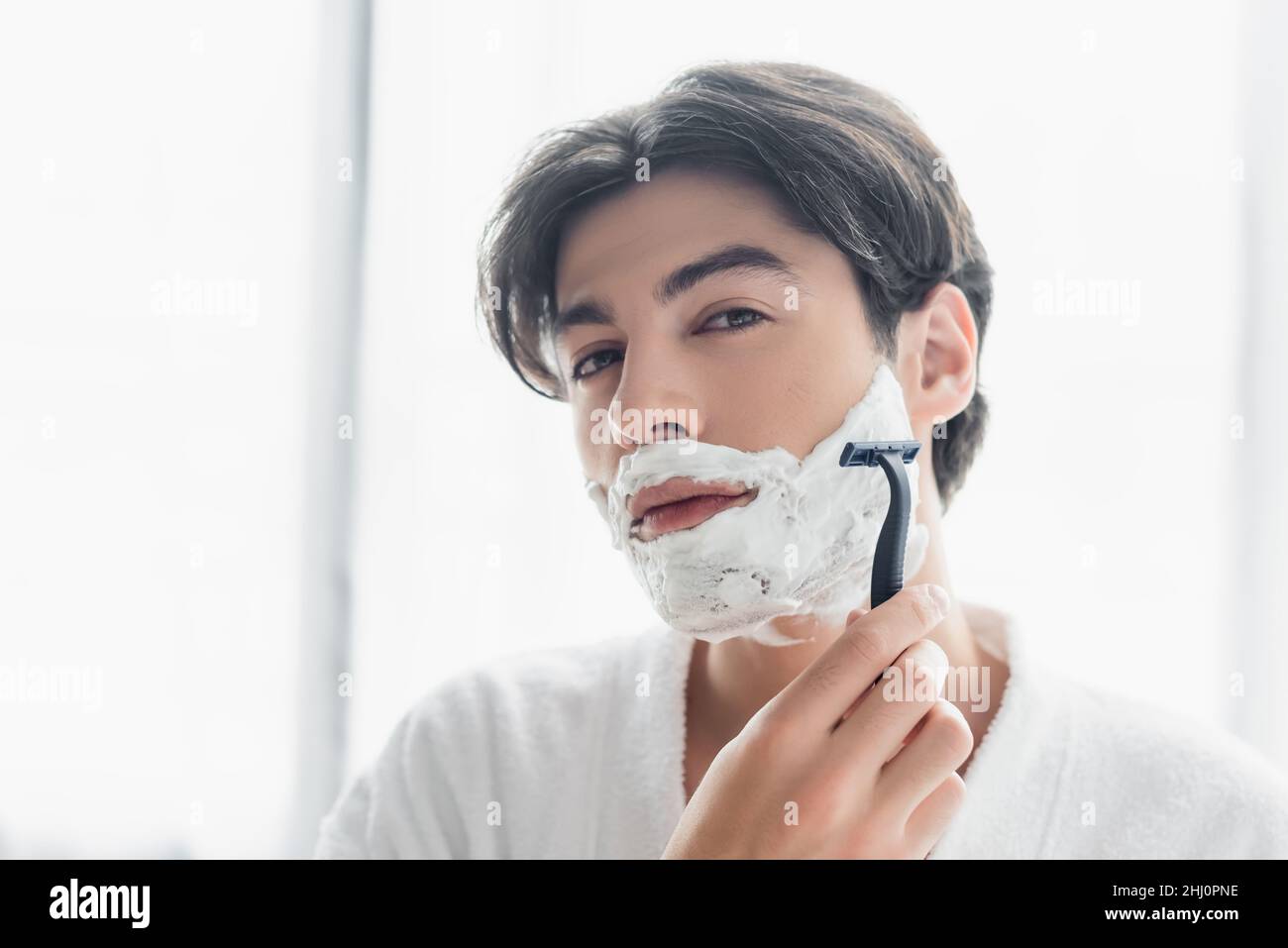 brunette man looking at camera while shaving with safety razor Stock ...