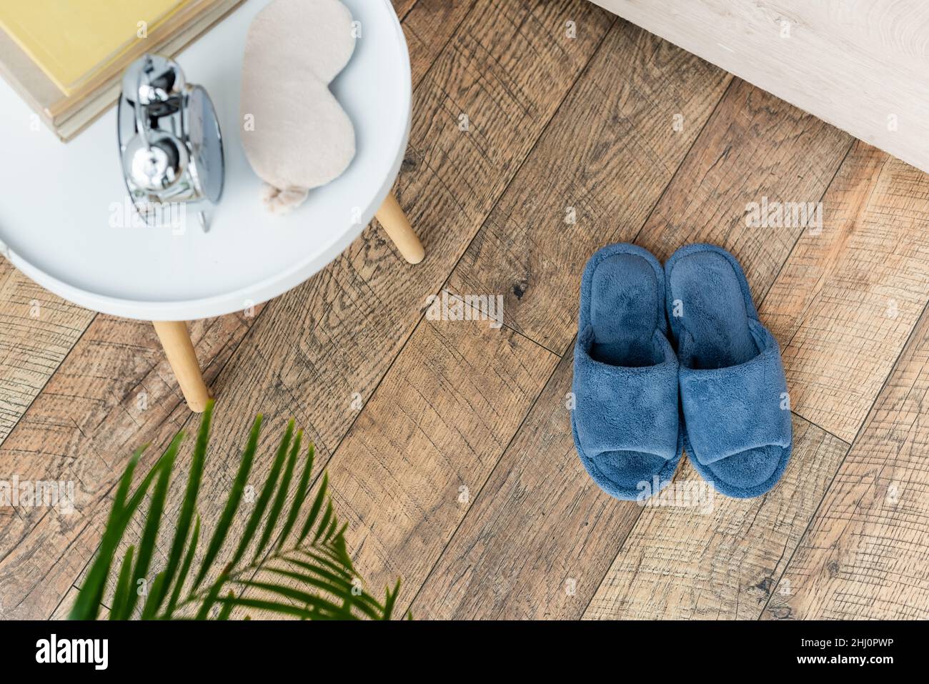 top view of soft slippers near bedside table with vintage alarm clock ...