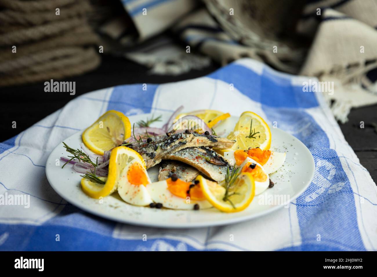 Herring fish fillets with eggs, herbs, onion and lemon on a white plate ...