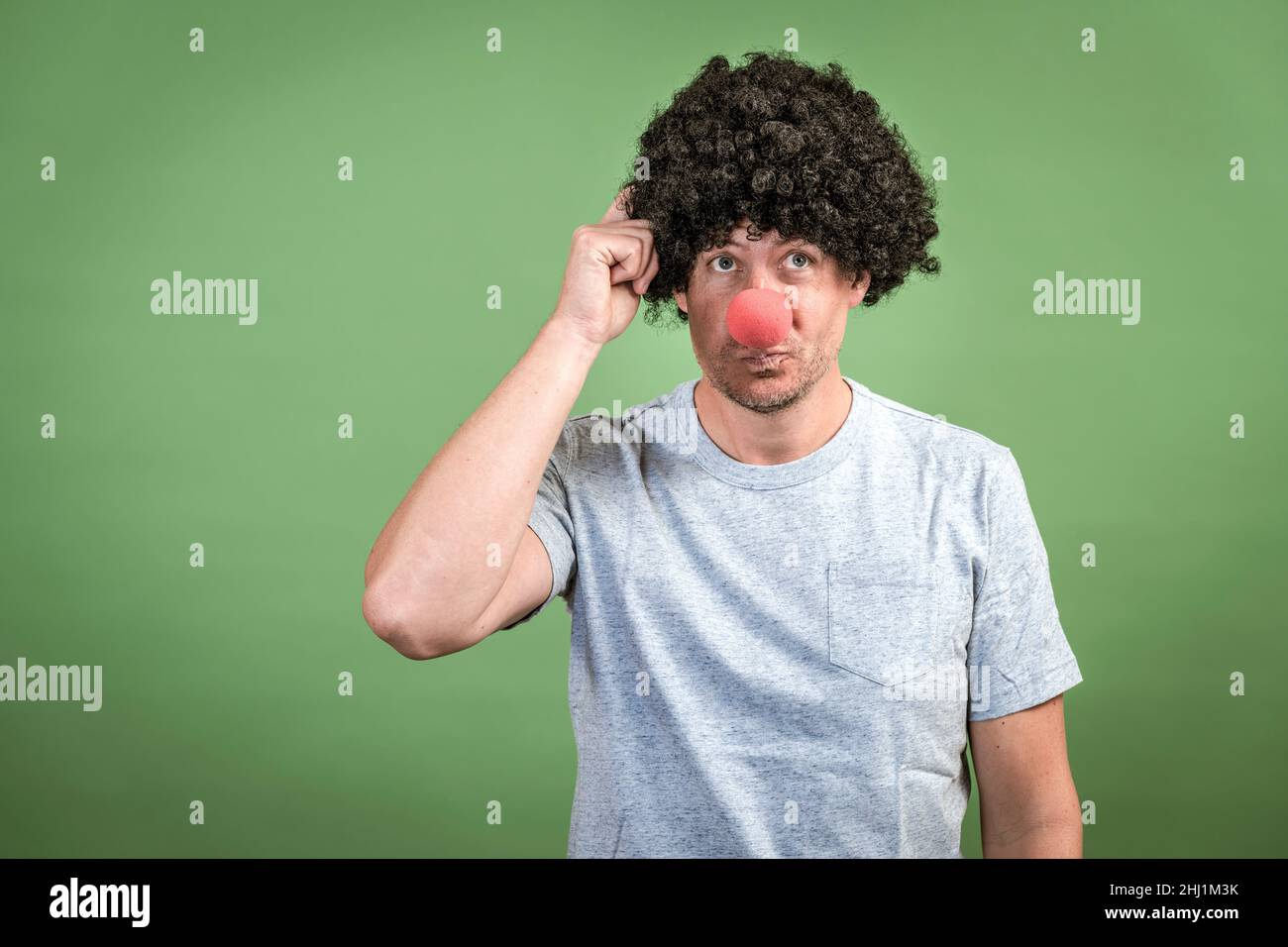 Man with black wig and red clown nose posing in front of green ...