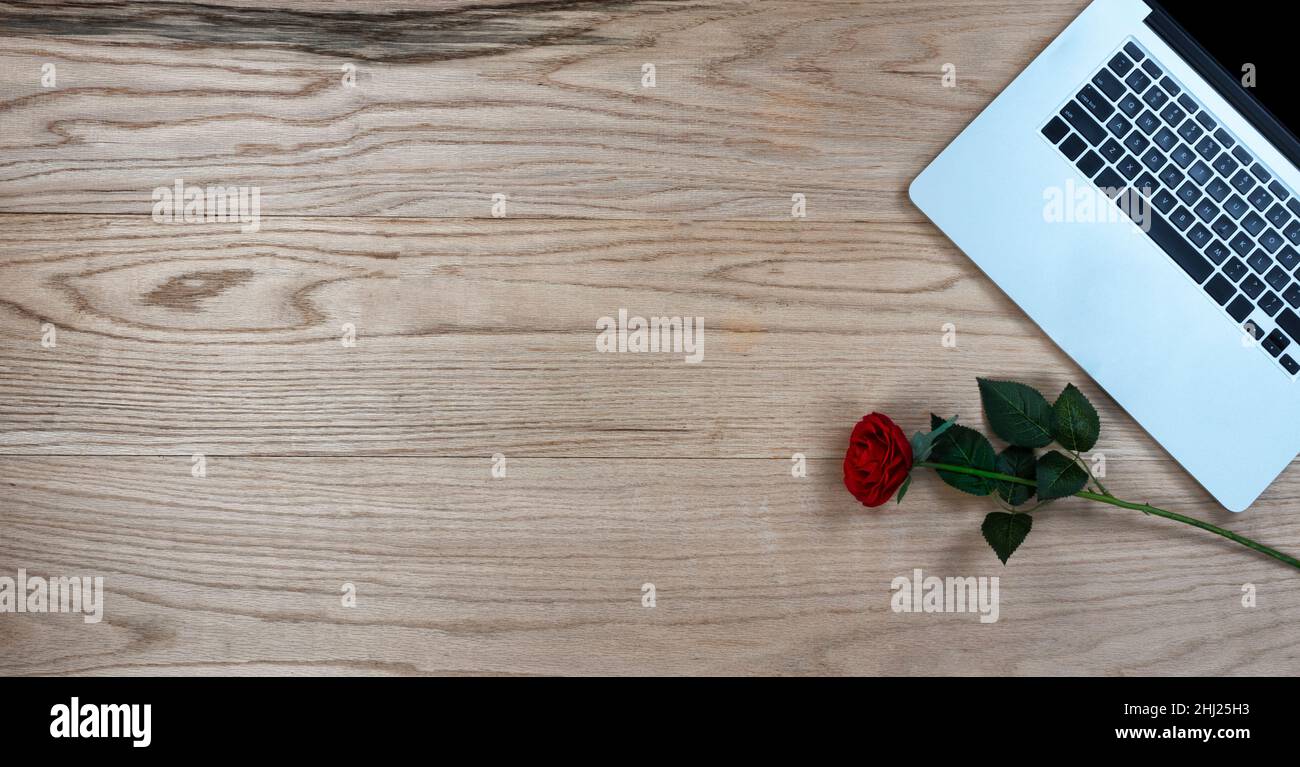 Oak wood office desk table with lovely red rose and a laptop computer ...