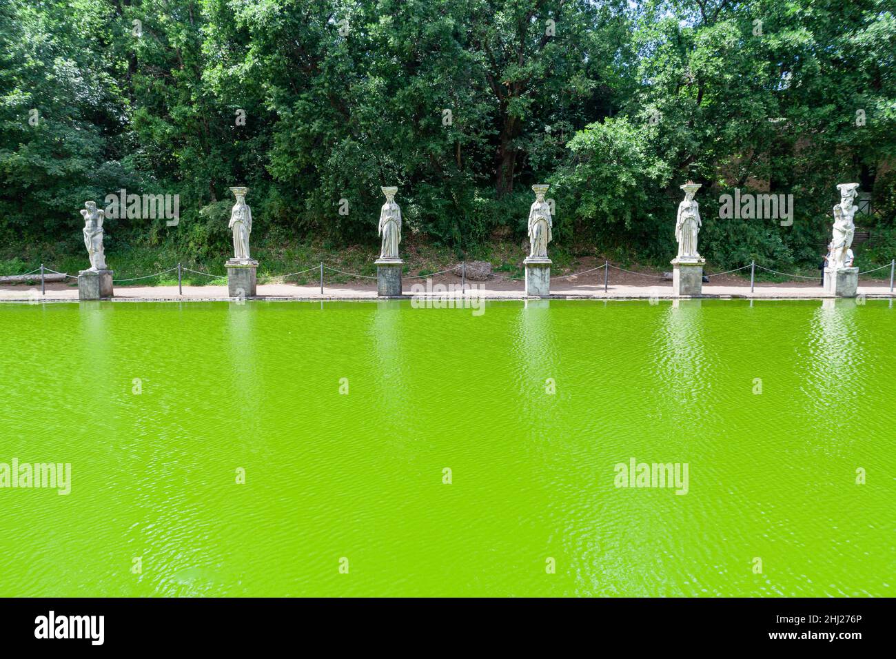 The green water of an ancient swimming pool surrounded by Roman statues ...