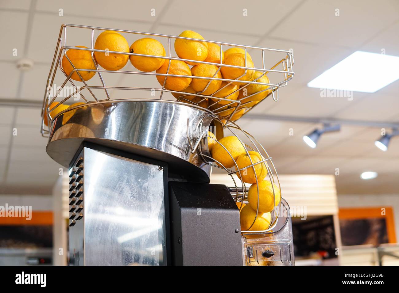 Fresh orange fruits in orange juice machine at store. Juicer in the ...