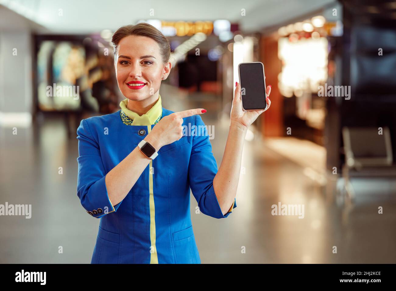 Joyful woman flight attendant pointing at smartphone at airport Stock ...