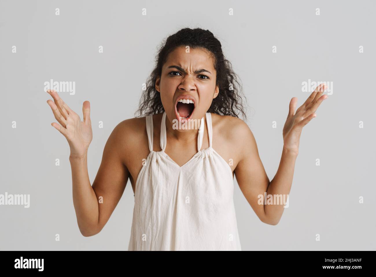 Black young woman screaming at camera with hands up isolated over white ...