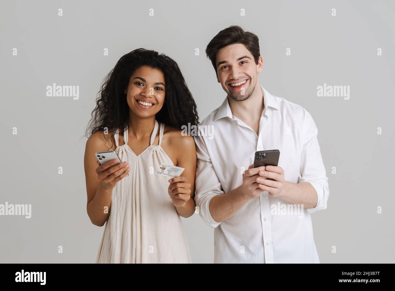 Young multiracial couple posing with cellphones and credit card ...