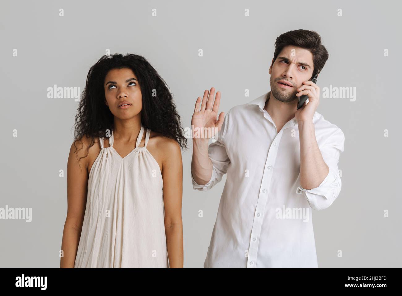 Young multiracial couple frowning while talking on mobile phone ...