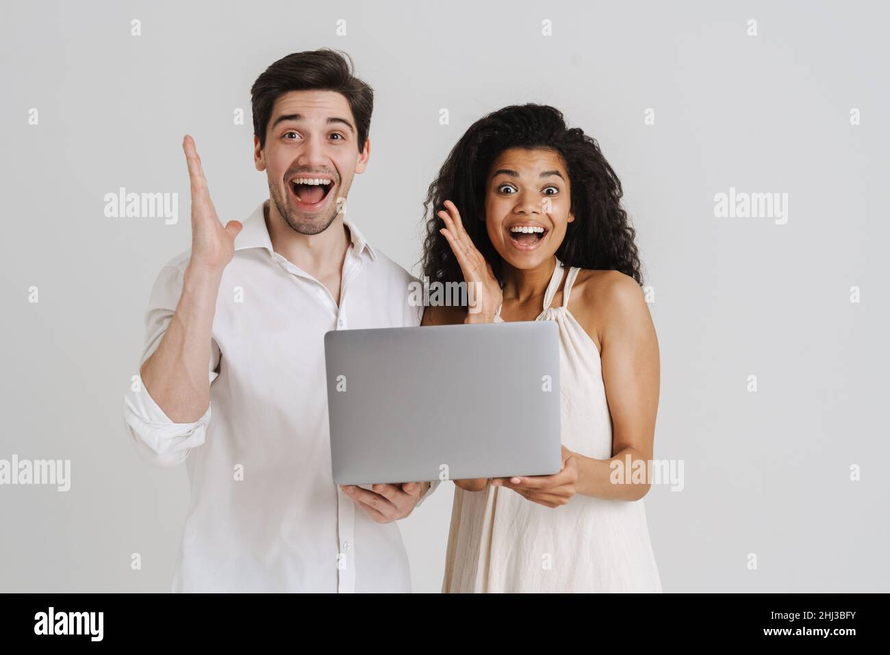 Multiracial excited couple posing with laptop and screaming isolated ...