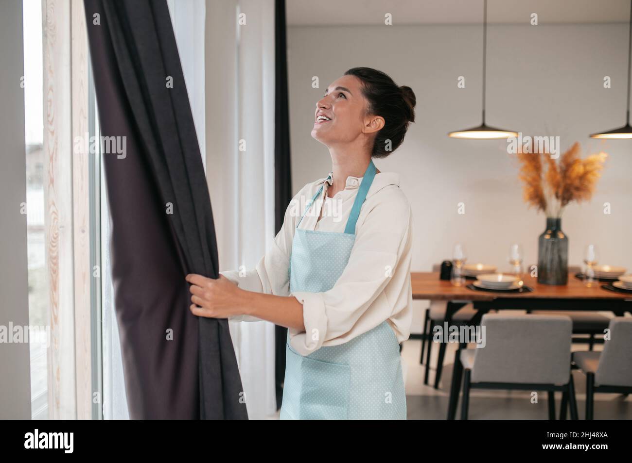 Young woman standing near the widnow and fixing the curtains Stock ...