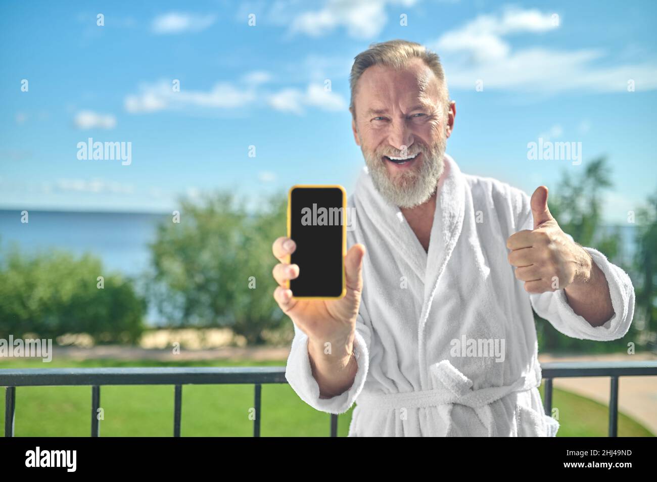 Happy gentleman in the white bathrobe demonstrating his smartphone ...