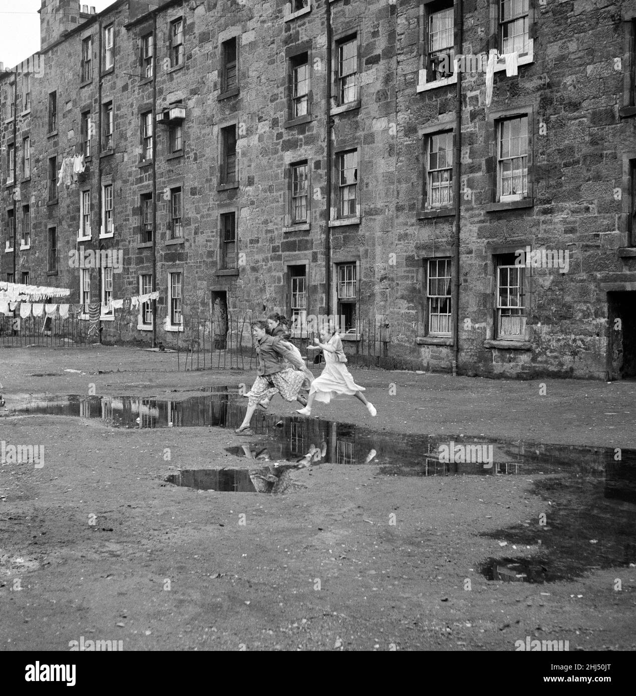 Three young friends leap over a puddle outside a Govan tenement block ...