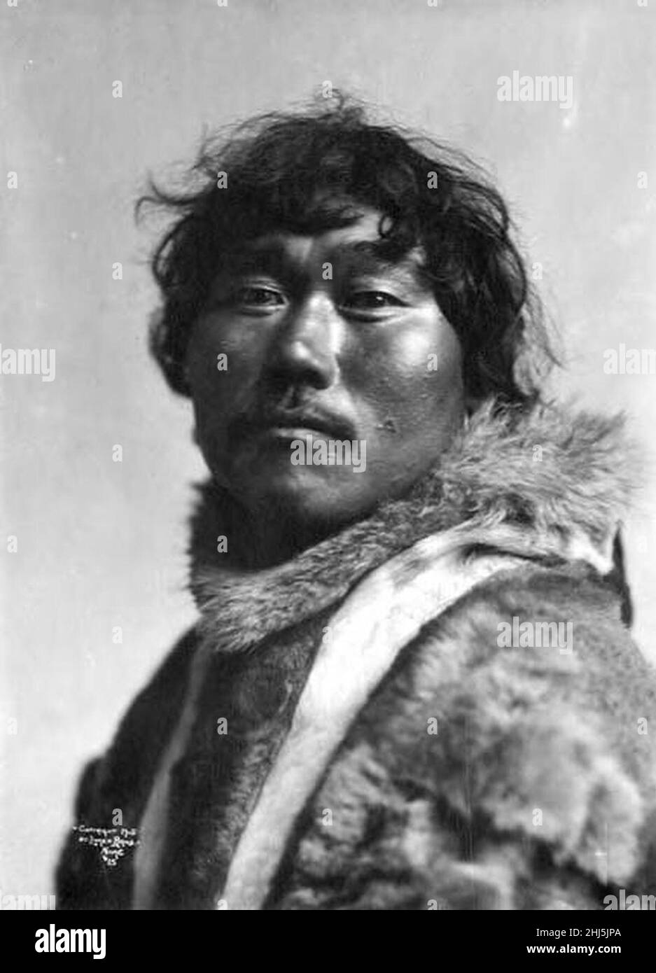 Studio portrait of Eskimo man with mustache and wavy hair in fur parka ...
