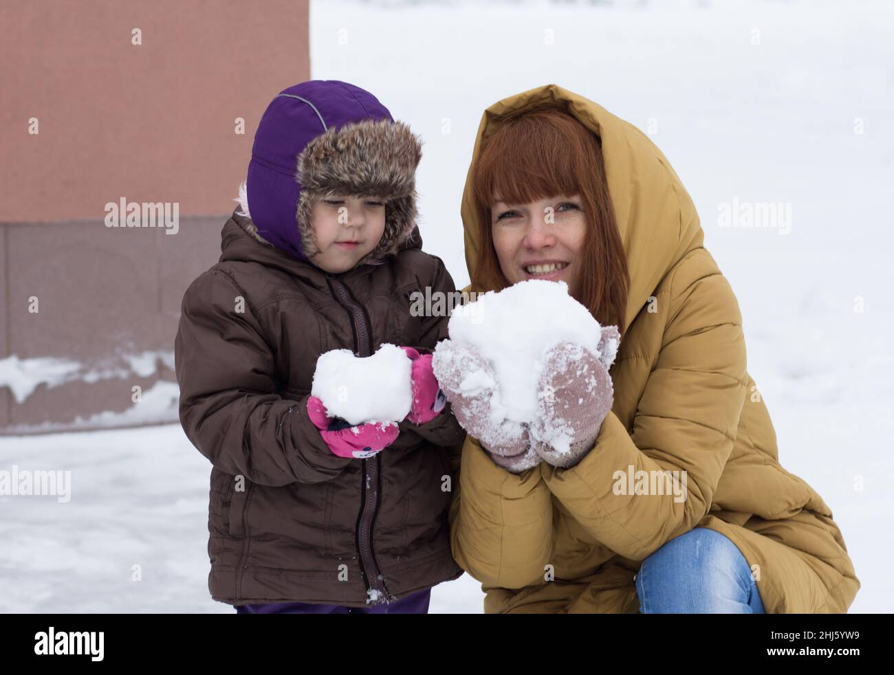 Mother and child of three years old holding snowballs in hands in ...