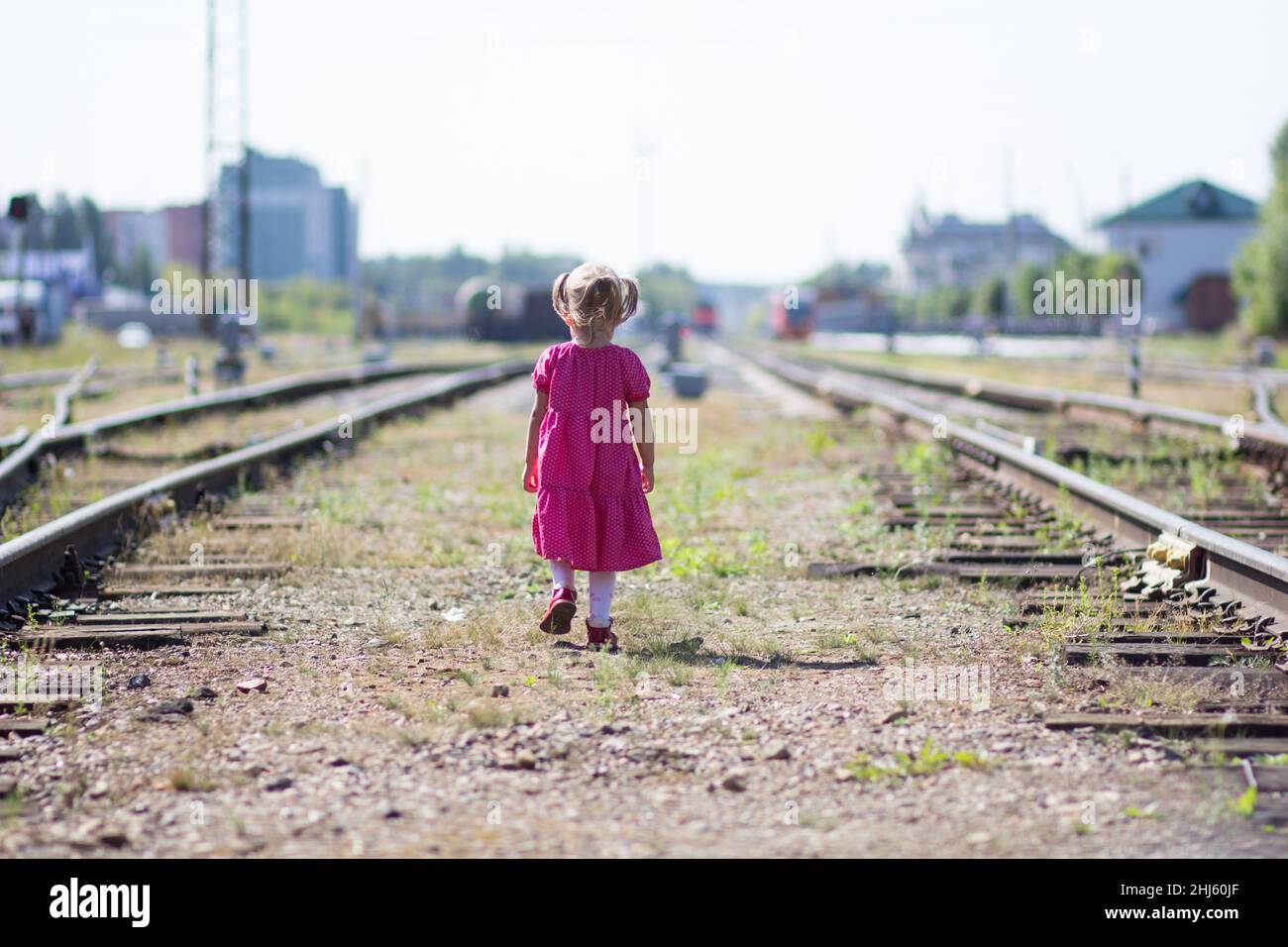Back of little girl walking alone among rails on railroad in summertime ...