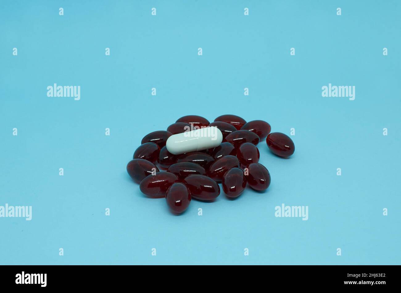 Many dark red capsules and one white capsule are scattered on a blue ...