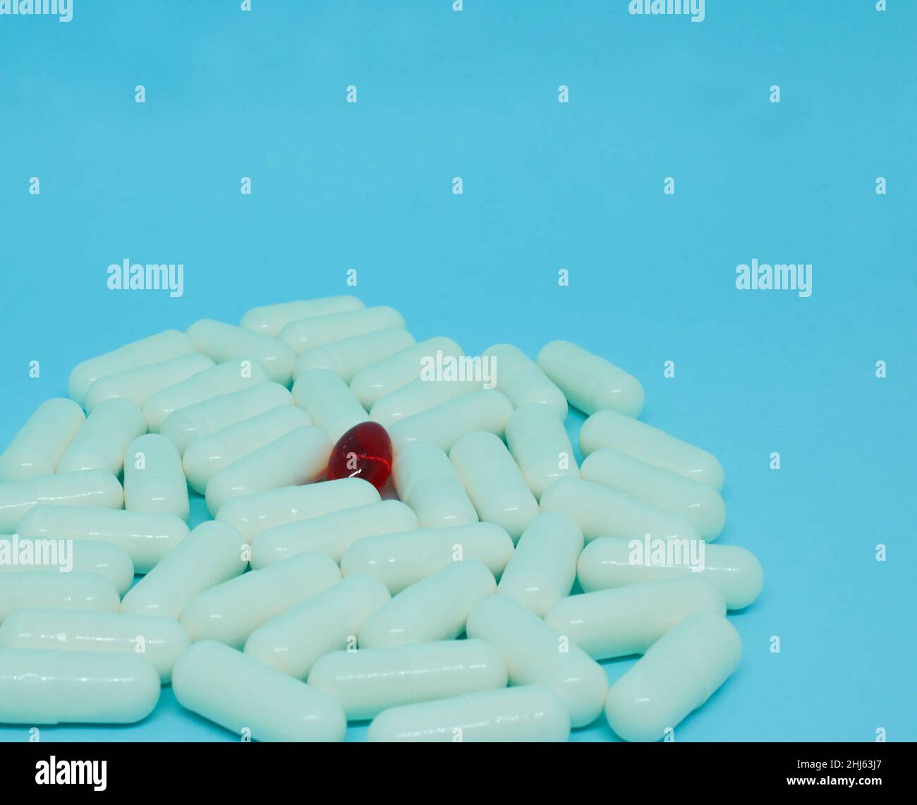 Many white capsules and one dark red capsule are scattered on a blue ...
