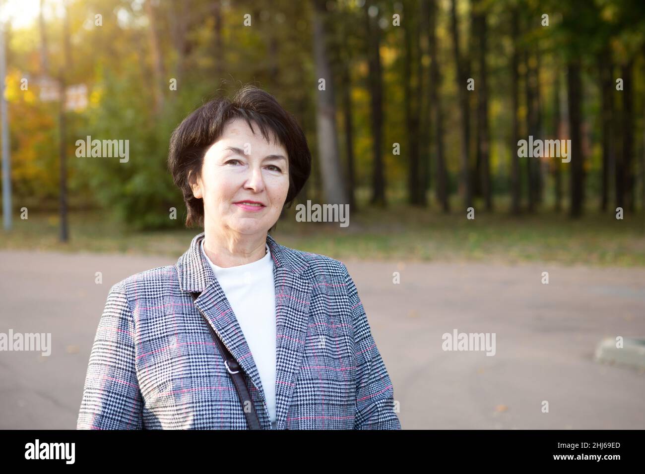 Portrait of a happy senora for 50 years in the park in autumn in a gray ...