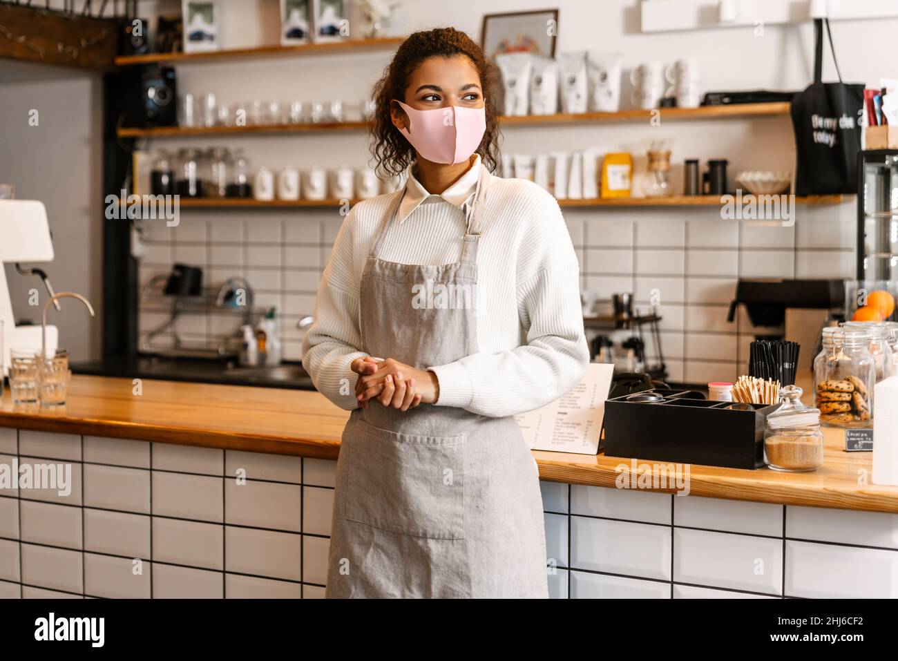 Young black waitress in face mask standing by cafe counter indoors ...