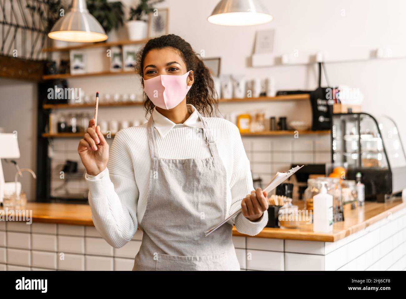 Young black waitress wearing face mask writing down notes on clipboard ...