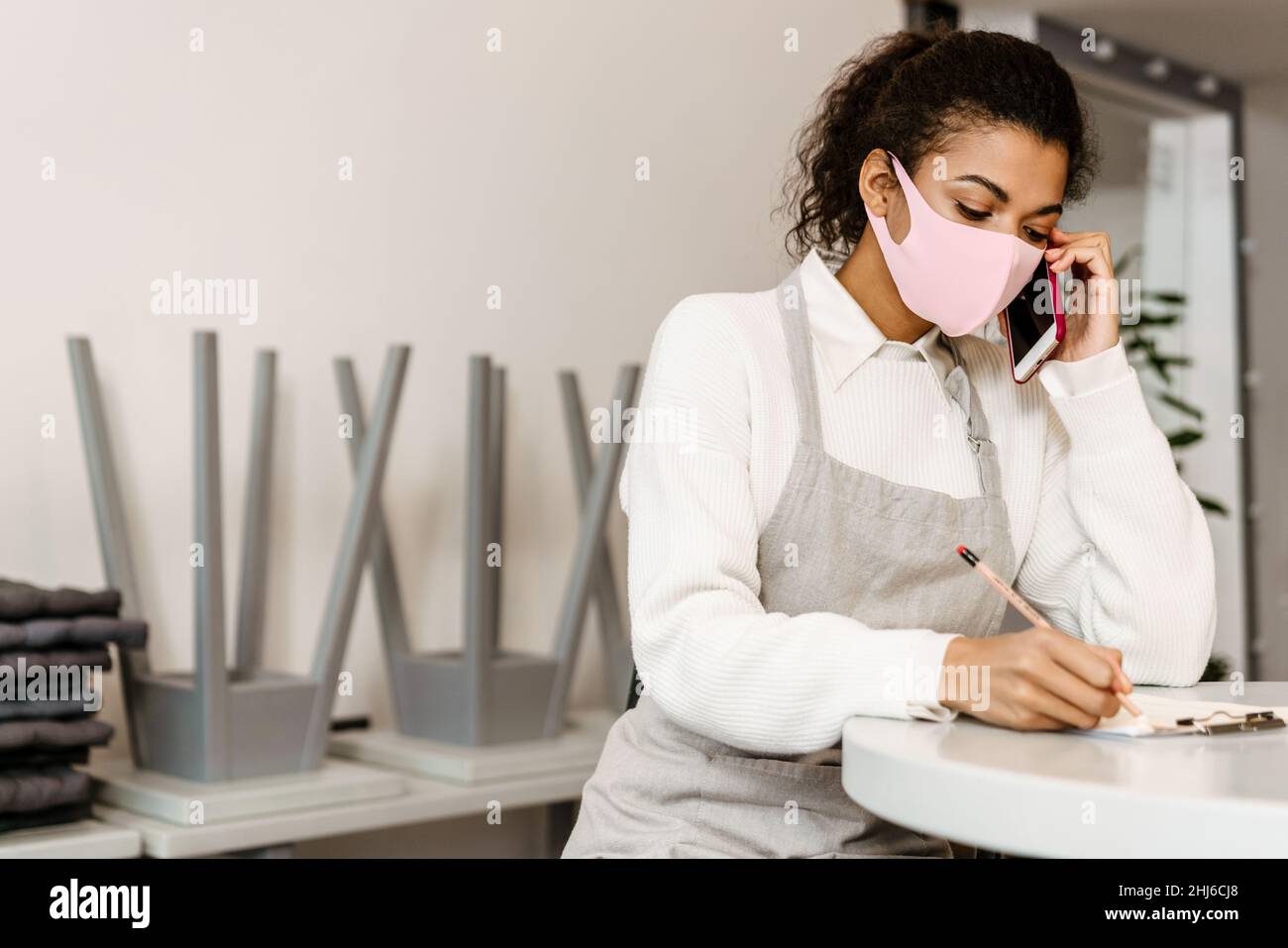Young black waitress wearing face mask talking on cellphone while ...