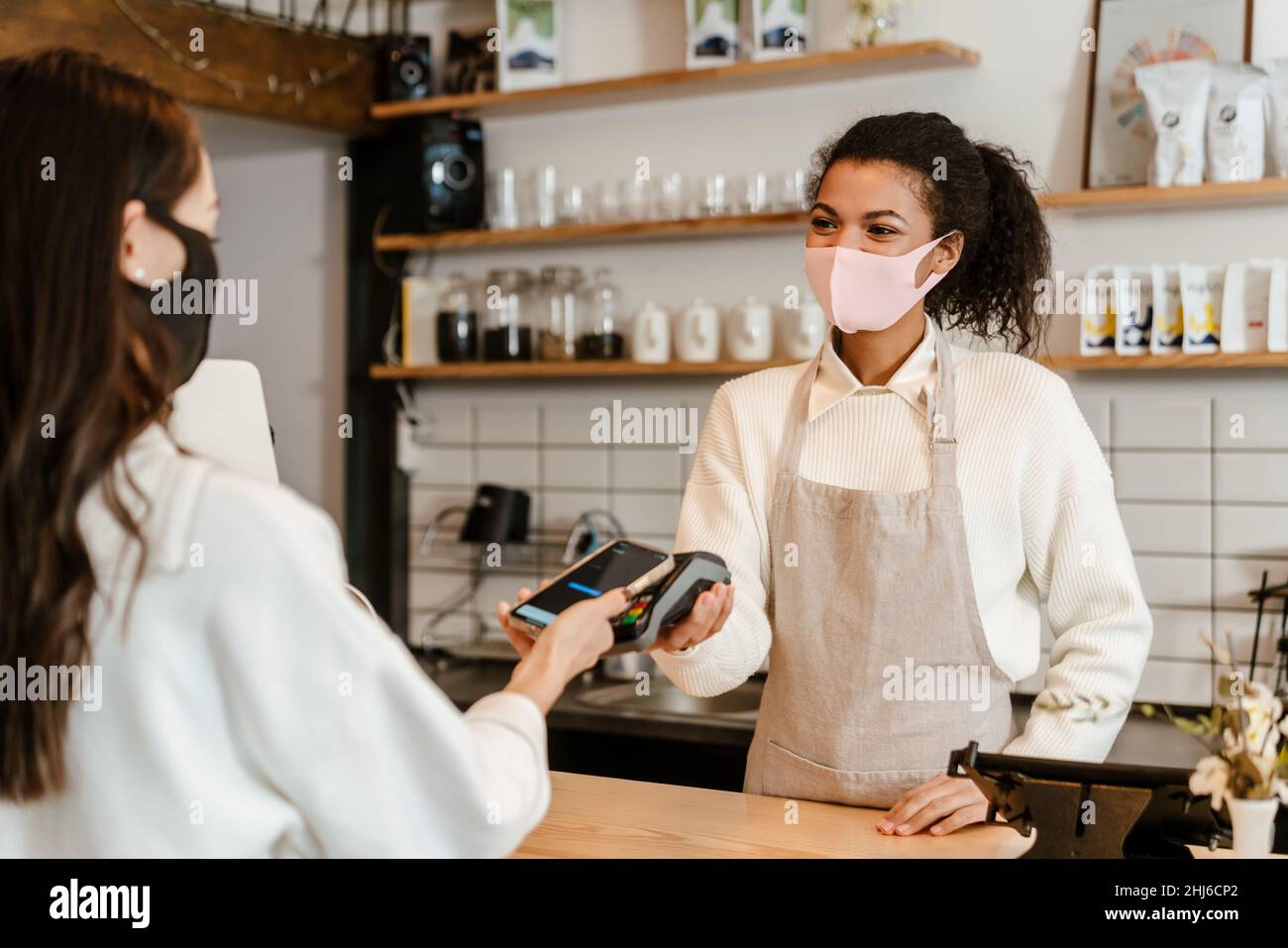 Young black waitress in face mask working with payment terminal at cafe ...