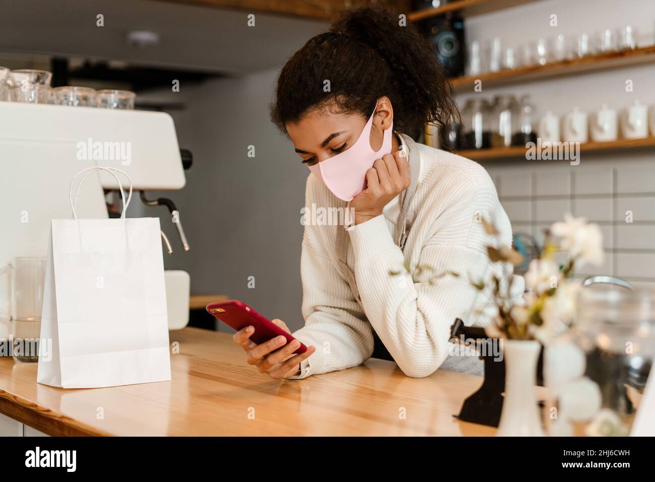 Young black waitress wearing face mask using cellphone while working in ...