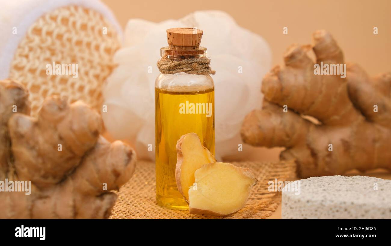 Glass bottle of essential ginger oil, ginger root on beige background ...