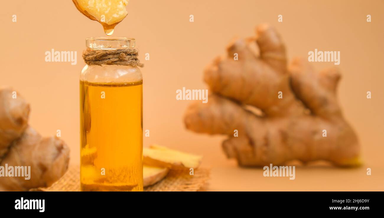 Glass bottle of essential ginger oil, ginger root on beige background ...