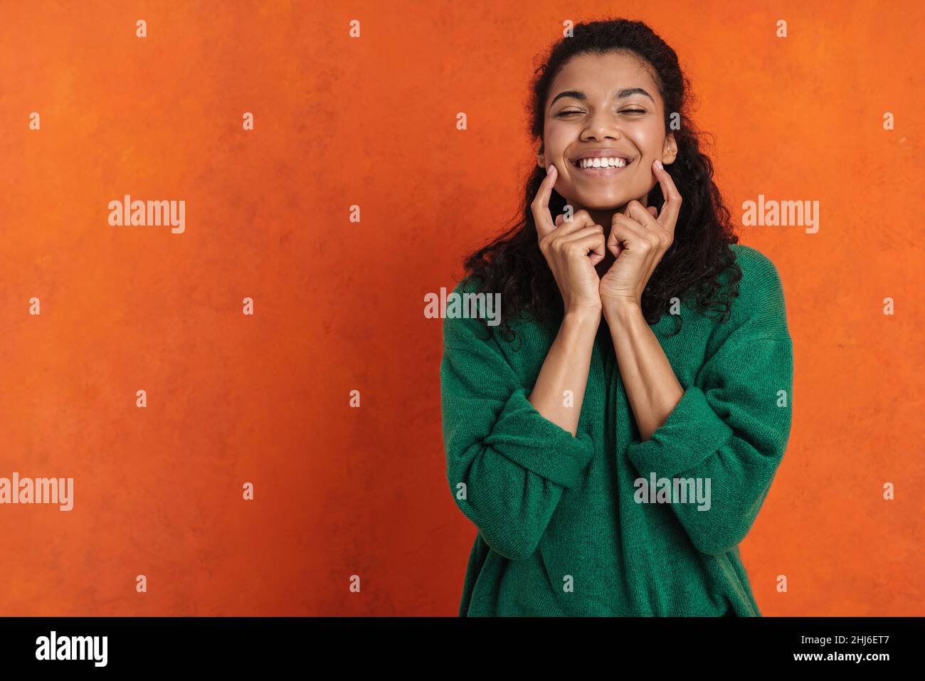 Happy smiling african casual brunette woman standing over orange wall background, grimacing ...