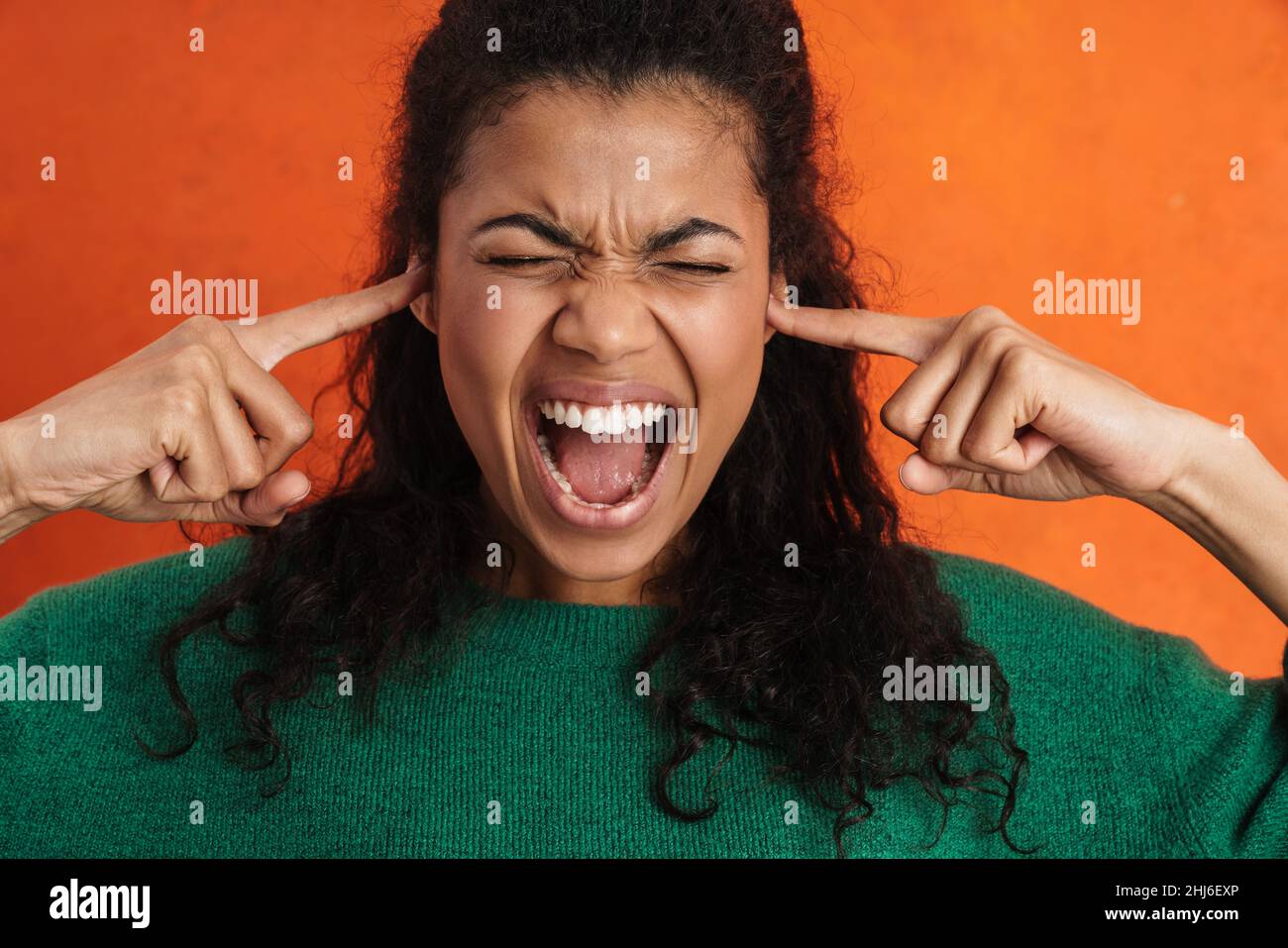 Frowning young african woman in casual wear standing over orange ...