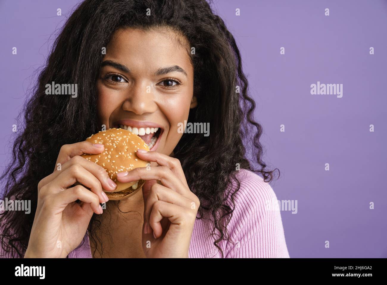 Young black woman with curly hair laughing while eating hamburger ...