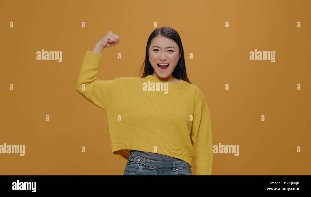Athletic woman flexing arms muscles over yellow background, showing ...