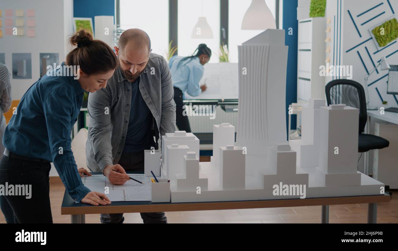 Workmates Analyzing Maquette And Blueprints Plan On Table To Work On Architecture And Building