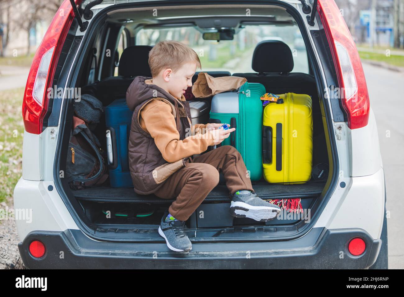 little kid looking into paper bag with candies sitting in car trunk ...