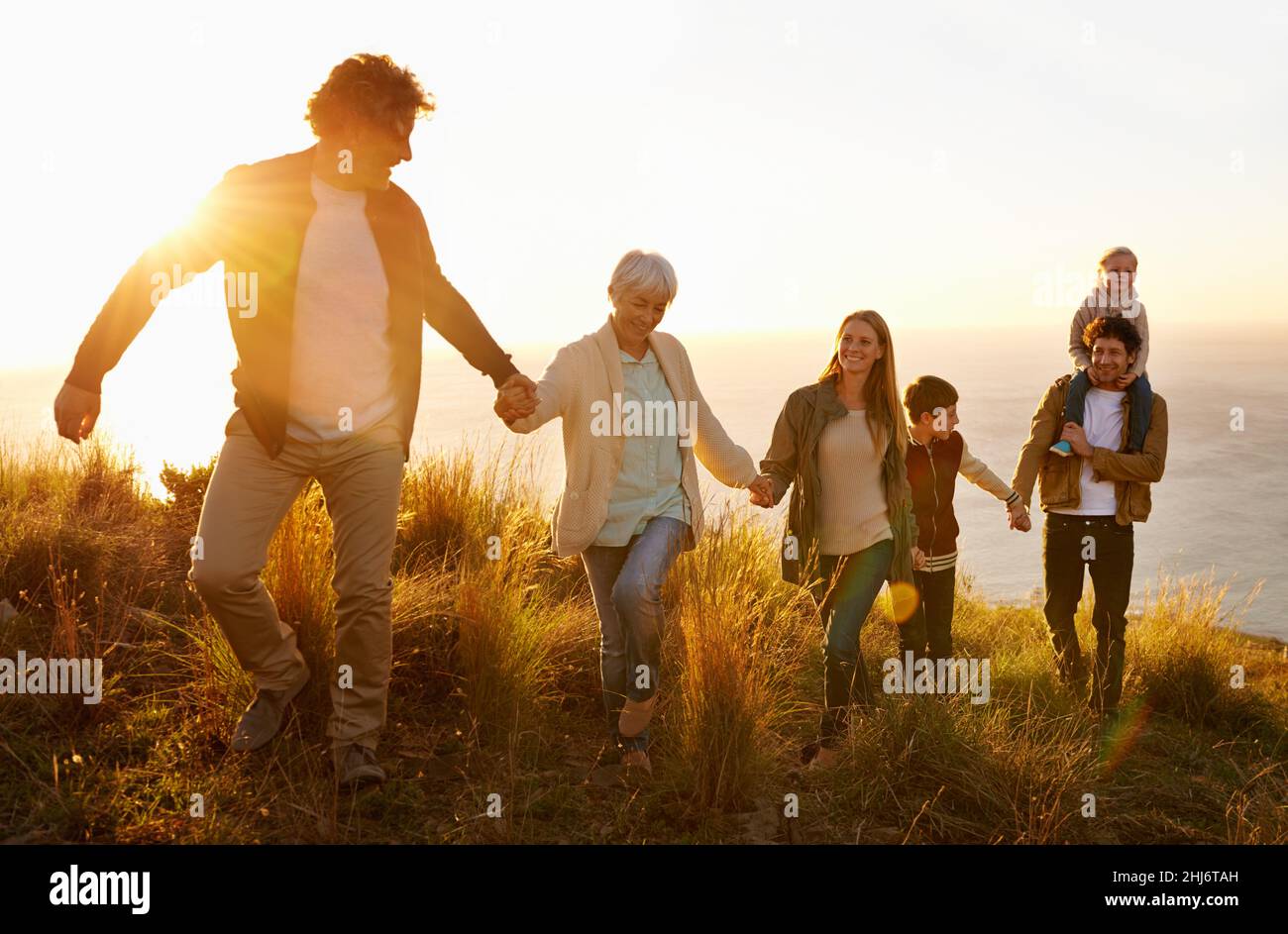 Family teamwork. A multi-generational family walking up a grassy hill ...