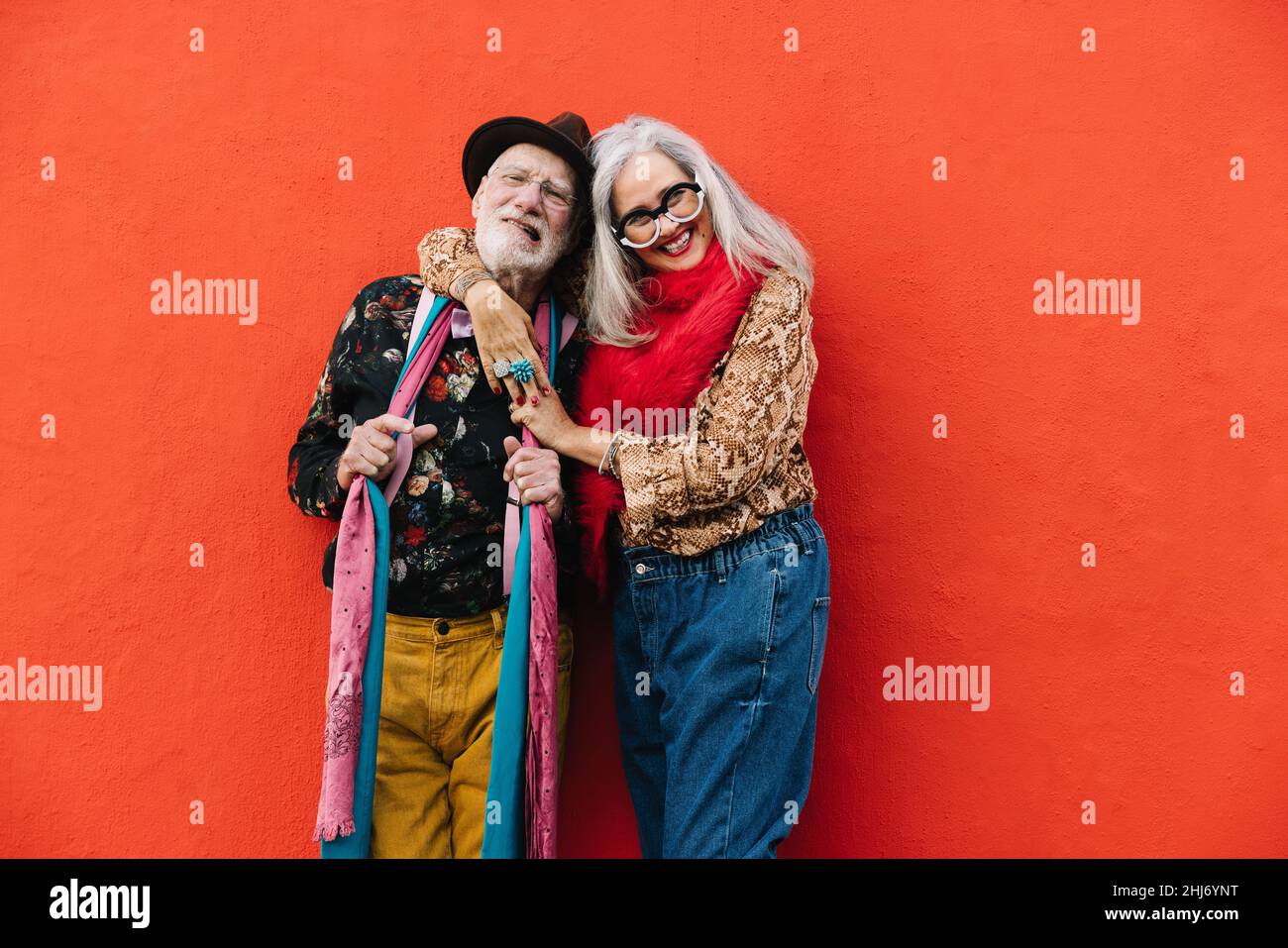 Happy senior couple smiling while standing together against a red ...