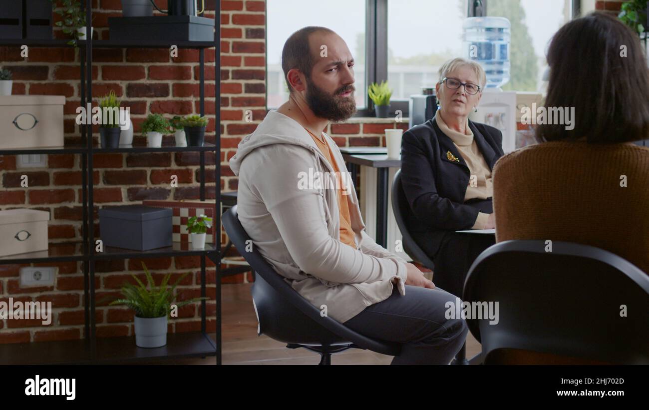 Frustrated man sharing story with group of people and therapist at aa ...