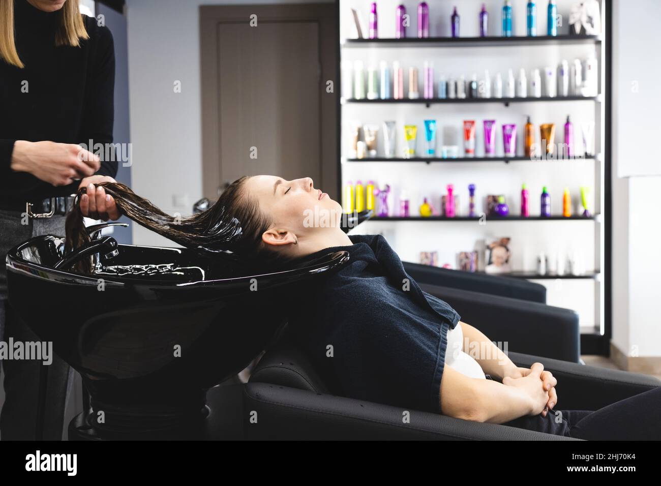 Master woman hairdresser gently washes the girl's hair with shampoo and ...