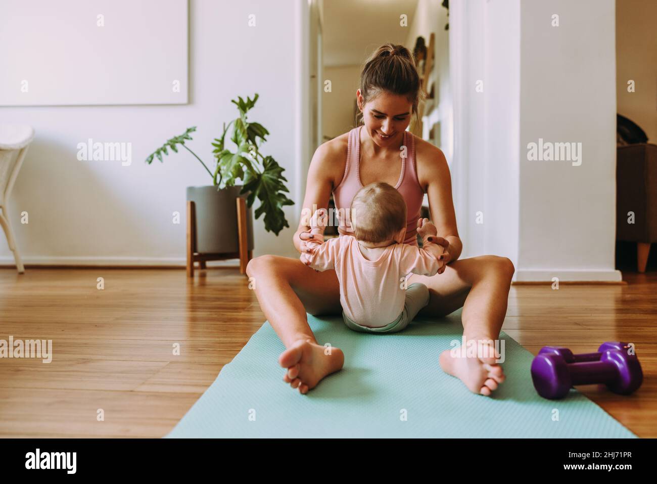 Cheerful mom working out with her baby on an exercise mat. Happy young mom doing sit up ...