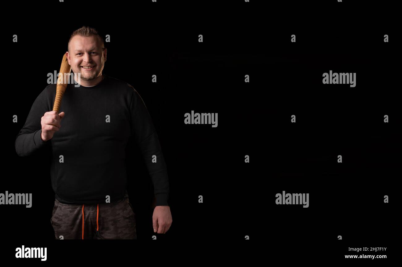 A young man holds a bat in his hand and smiles. Dark background. Place ...