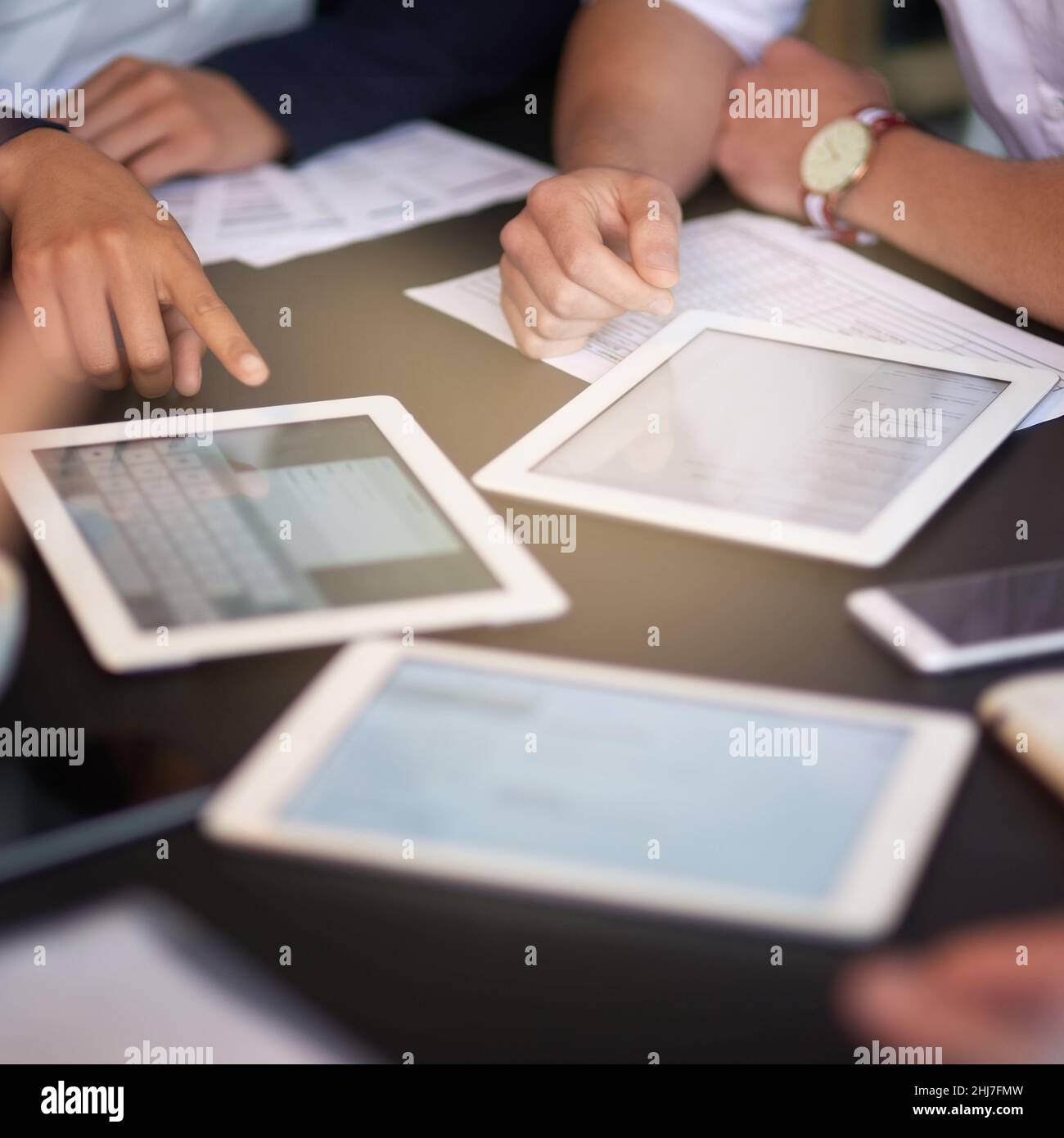Syncing the team's devices. Closeup shot of a group of professionals ...